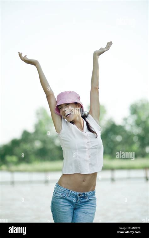 Woman Standing With Arms Raised Showing Bare Midriff Smiling At