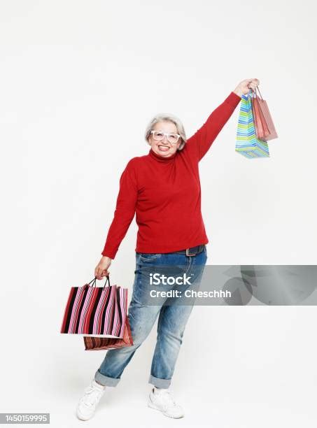 긍정적 인 쾌활한 회색 흰 머리 노인 여성의 전체 길이 사진은 여가 시간 쇼핑 홀드 가방을 청바지와 빨간 스웨터를 착용 65 69세에 대한 스톡 사진 및 기타 이미지