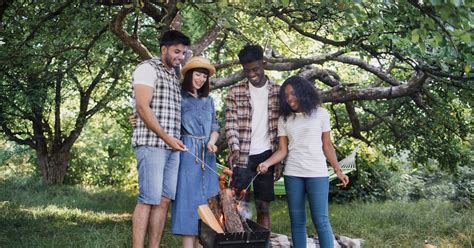 소시지를 굽기 위해 바베큐 주위에 모인 4 명의 다문화 친구들 여름 옷을 입은 젊은이들이 야외에서 불에 음식을 요리하고 있습니다 사진 Unsplash의 우크라이나 이미지