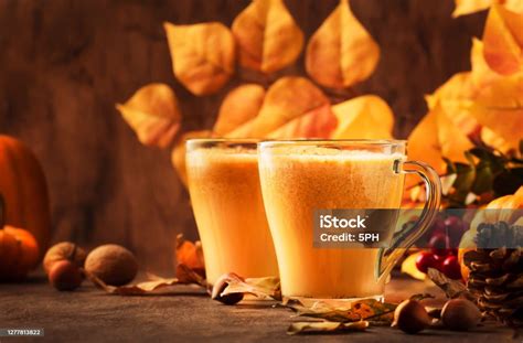 빈티지 나무 테이블에 유리 컵에 호박 향신료 라떼 또는 커피 가을 또는 겨울 따뜻한 음료와 음료 낙엽 작은 호박 소나무 콘 견과류가 있는 가을 장식 테이블 설정 위스키에