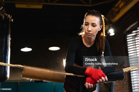 여자 파이터 걸 파워 빨간 권투를 한 여자 파이터는 권투 링에 서서 보호 붕대를 감고 밧줄에 기대어 휴식을 취합니다 강한 강력한 소녀 근력 운동 운동에 적합합니다 30 34