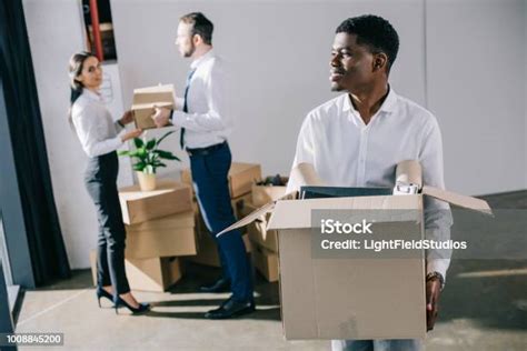 새로운 사무실에서 동료 들과 함께 이전 하는 동안 골 판지 상자를 들고 웃는 아프리카계 미국인 실업가 경영자에 대한 스톡 사진