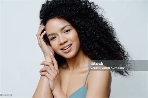 뷰티 스킨 케어 컨셉 아프로 머리를 가진 아름다운 부드러운 젊은 여성은 건강 잘 돌보는 피부를 가지고 머리를 만지고 카메라에 긍정적으로 보이는 흰색 배경에 고립 된 맨