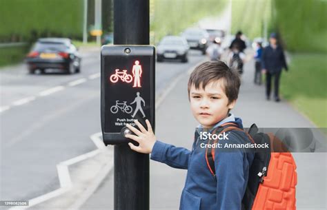 학교 아이는 학교로가는 길에 횡단하는 보행자의 신호등에서 버튼을 누릅니다 교통 신호를 사용하여 배낭을 가진 어린이 소년은 도로를 건너기 위해 보행자 시설을 제어했습니다