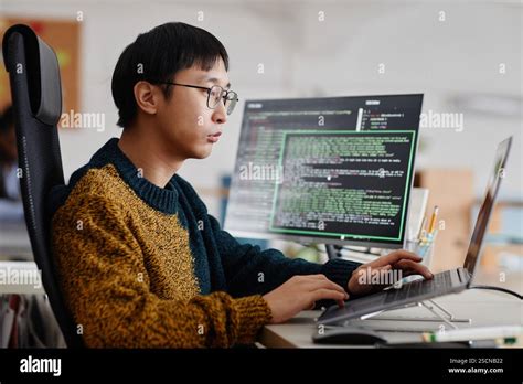 Man Concentrating On Writing Code At Workstation With Multiple Screens Displaying Programming