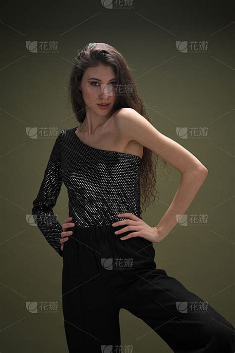 一个美丽的年轻高个女孩与黑色长发摆姿势在绿色背景上一件闪亮的衬衫和黑色的裤裙Buty和时尚摄影