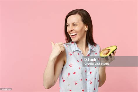 여름 옷을 옆에 젊은 여자를 웃 고 밖으로 분홍색 파스텔 배경에 고립 된 신선한 잘 익은 아보카도 과일의 절반을 잡아 사람들은 생생한 라이프 스타일 휴식 휴가 개념입니다
