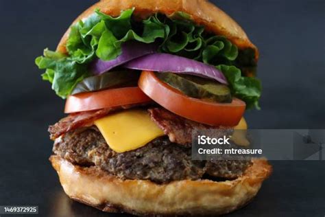 빵 롤빵 햄버거 패티 베이컨 러셔 녹는 가공 치즈 조각 양상추 잎 얇게 썬 토마토 피클과 붉은 양파 조각 검은색 배경 전경에