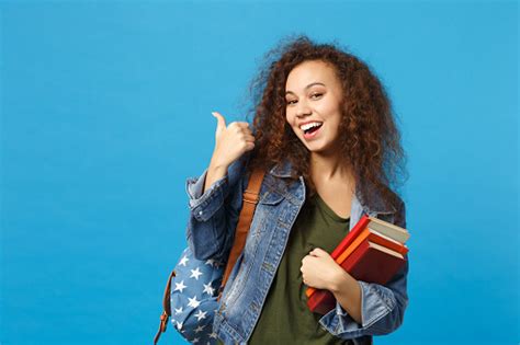 데님 옷에 젊은 아프리카계 미국인 소녀 사춘기 학생 배낭은 파란색 벽 배경 스튜디오 초상화에 고립 된 책을 잡아 고등학교 대학