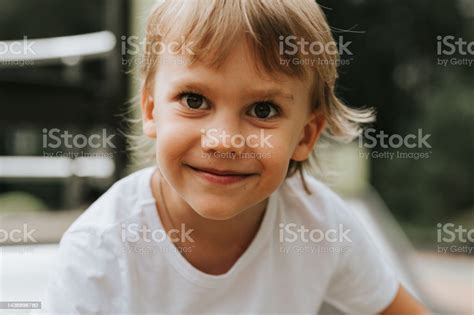 흰색 티셔츠에 큰 눈과 긴 금발 머리를 가진 귀여운 행복한 미소를 짓는 솔직한 다섯 살 소년의 얼굴 초상화 Z 세대 어린이 정신