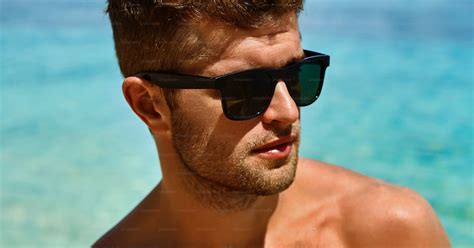 여름에 남자 스킨 케어 선글라스를 끼고 섹시한 몸매를 가진 잘생긴 남성이 일광욕을 하기 전에 자외선 차단 자외선 차단제 로션을 바르고 건강한 황갈색을 위해 태양 자외선