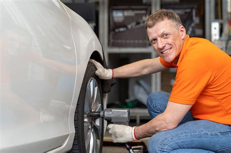 자동차 수리점에서 자동차의 공압 렌치 변하는 타이어를 사용하는 남성 정비사 볼트를 풀어주는 전기 드릴로 자동차의 전문 정비사