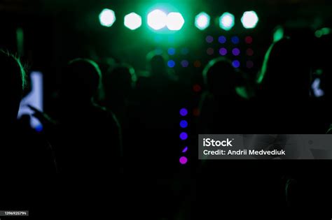 밝은 파란색 녹색 무대 조명 앞에서 환호하는 군중 사람들의 실루엣 이미지는 디스코 나이트 클럽이나 음악 축제에서 콘서트에서 춤을 추고 있습니다 전경에 대한 스톡 사진 및