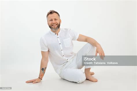웃고 있는 잘생긴 중년 수염 난 남자가 짧은 회색 머리를 하고 흰색 배경에 바닥에 다리를 꼬고 앉아 있다 중장년에 대한 스톡 사진 및 기타 이미지 Istock