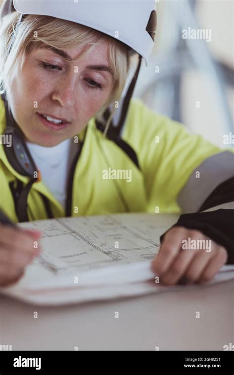 Female Building Contractor Writing While Analyzing Floor Plan At Construction Site Stock Photo