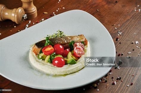 흰 접시에 육즙이 많은 연어 스테이크와 으깬 감자 아보카도 체리 토마토와 녹색 소스를 곁들인 반찬이 나옵니다 나무 배경입니다 맛있는 레스토랑 해산물을 가까이에서 맛보세요 0