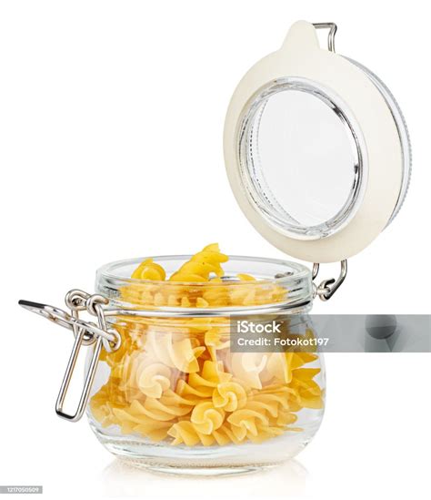 흰색 배경에 분리 된 뚜껑에 고무 밀봉 및 금속 클램프가있는 열린 투명 유리 항아리에 말린 이탈리아 파스타 나선형 Fusilli