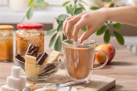 소년의 손은 우유와 차 또는 커피 한 잔 위에 설탕 큐브를 들고있다 다양한 종류의 과자와 설탕이 식탁에 놓여 있습니다 꿀에 대한