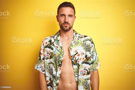얼굴에 심각한 표정으로 노란색 고립 된 배경 위에 여름 하와이 꽃 셔츠를 입은 잘 생긴 남자 카메라를 보는 간단하고 자연스러운 결심에 대한 스톡 사진 및 기타 이미지