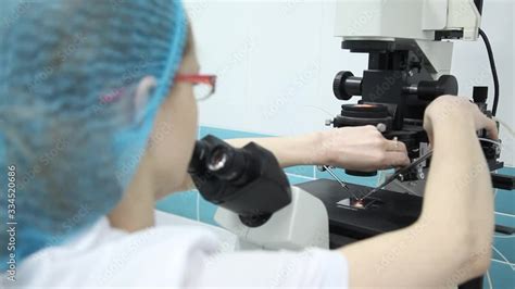 A Medical Worker Woman Sitting At A Large Microscope And Analysesthe