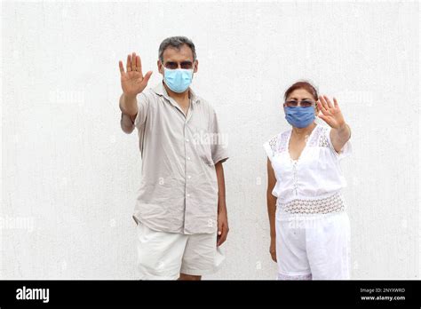 Older Latino Couple With Protective Face Masks On White Wall Background