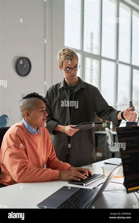 Vertical Image Of Young Colleagues Discussing Codes Of Software Pointing At Computer Monitor