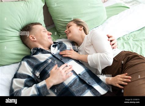 A Young Man And Woman Lie Comfortably On A Bed Sharing A Close