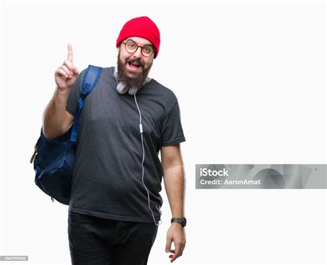 젊은 Hipster 남자 성공적인 아이디어와 손가락 가리키는 격리 된 배경 위에 빨간 모직 모자와 가방 입고 종료 하 고 행복 번호 하나입니다 과체중에 대한 스톡 사진 및