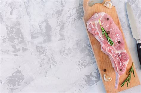 생고기의 조각이 커팅 보드에 놓여 있습니다 후추와 로즈마리가 있는 돼지고기 스테이크 회색 돌 배경에 공간을 복사 합니다 텍스트에