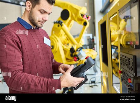 Engineer Working On Programming An Industrial Robot With A Gripper Arm In A Factory Setting