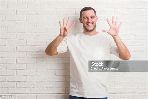 젊은 백인 남자를 표시 하 고 손가락으로 가리키는 흰색 벽돌 벽을 통해 서 자신감과 행복 미소 동안 9 번호 가리키기에 대한