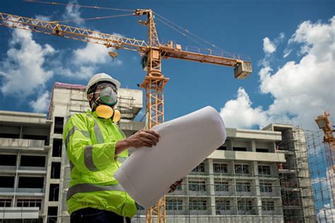 건설 현장에서 얼굴 마스크와 안전 헬멧을 착용한 토목공학인들이 청사진을 손에 들고 있다 건물 관리자 건설 현장 점검 도면 및