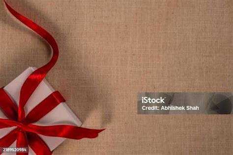 왼쪽 상단 모서리에 흰색 선물 상자가 있는 베이지색 질감의 배경에 빨간 리본 리본으로 묶여 있음 미적 모의 사진 배경 0명에