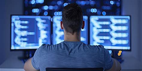 A Man Sits In Front Of Computer Screens Displaying Code In Blur