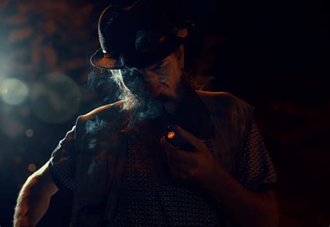 모자를 쓴 늙은 카리스마 넘치는 남자는 밤에 어두운 거리에서 파이프를 피운다 흡연에 대한 스톡 사진 및 기타 이미지 흡연