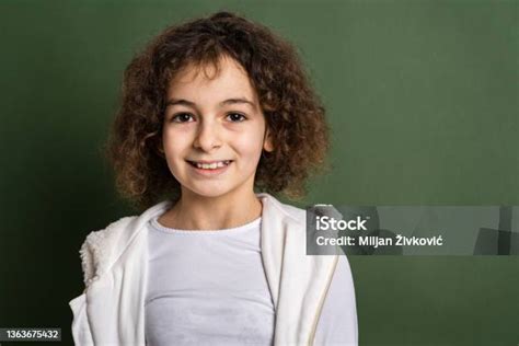 곱슬 머리 정면보기 초상화를 가진 열 살짜리 작은 백인 소녀 한 명이 녹색 배경 앞에 서서 행복하고 기쁨의 복사 공간을 웃고있는 카메라를 바라 봅니다 10 11세에 대한