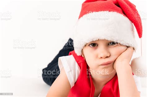 흰색 배경에 고립 된 빨간 산타 클로스 모자에 누워 분개 어린 아이의 클로즈 업 초상화 아름다운 5 년 유럽 소년 선물을 기다립니다 공간을 복사합니다 즐거운 성탄절 기분이