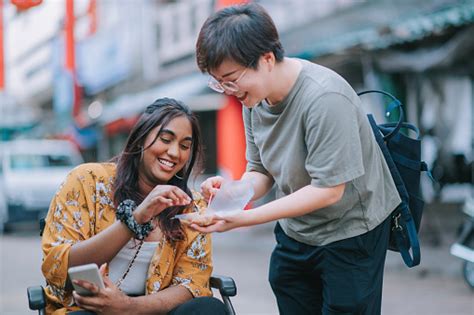 휠체어에 앉아 있는 장애가 있는 아시아 인디언 여성 중국 친구가 모찌 현지 길거리 음식을 즐기고 있다 장애에 대한 스톡 사진 및 기타 이미지 Istock