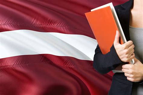 라트비아어 언어 개념을 학습 합니다 백그라운드에서 라트비아 국기와 함께 서 있는 젊은 여자 책을 들고 교사 오렌지 빈 책 표지