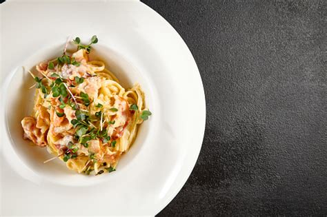 어두운 배경에 흰색 접시에 바삭한 베이컨과 신선한 마이크로그린을 얹은 크리미한 까르보나라 파스타 Comfort Food에 대한