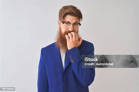젊은 빨간 머리 아일랜드어 사업가 는 입물고 손톱에 손을 긴장 찾고 고립 된 흰색 배경 위에 양복과 안경을 착용 불안 문제
