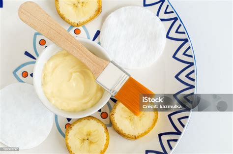 작은 흰색 그릇에 디 바나나와 요구르트 마스크 메이크업 브러시 면 패드와 바나나 조각 천연 수 제 헤어 트리트먼트 와 제로 폐기물 개념 맨 위 보기 복사 공간n 바나나에