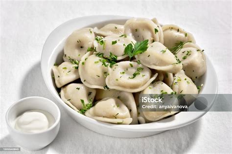 흰 그릇에 삶은 펠메니 펠메니는 얇은 밀 반죽에 싸여 다진 만남 과 수제 파스타입니다 사이드에 작은 세라믹 핀치 그릇에 사워