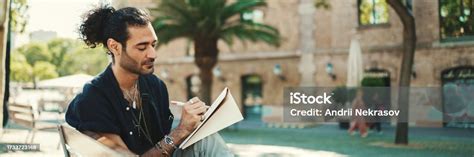 포니 테일과 그루터기를 가진 젊은 이탈리아 남자가 거리 벤치에 앉아서 종이에 펜으로 스케치를합니다 감정에 대한 스톡 사진 및 기타 이미지 Istock