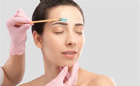 메이크업 아티스트는 얼굴 제모 절차를 수행합니다 그녀의 눈썹에 영구적 인 메이크업을 갖는 푸른 눈을 가진 아름다운 소녀 프로 메이크업 아티스트는 얼굴 제모 절차를 수행합니다