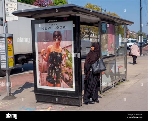 A Muslim Woman Waits At A Bus Stop Next To A Poster For Fashion Company