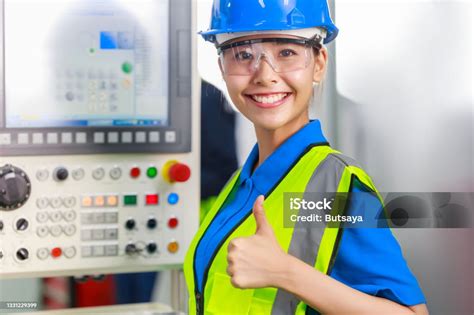 강철 공장에서 웃는 얼굴을 가진 기계 제어판 앞에 엄지 손가락을 보여주는 카메라를 보고 있는 보호 안경을 착용한 젊은 엔지니어 공장 노동자 여성 20 24세에 대한 스톡