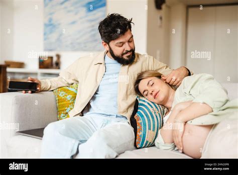 Bearded Man Caressing His Pregnant Wife While She Sleeping On Couch At