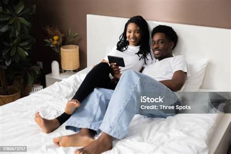 기뻐하는 사랑스러운 귀여운 아프리카 미국 여성 포옹 잘생긴 검은 피부 남편 침대에 누워 핸드폰을 들고 친구 가족과 화상 회의 좋은 분위기에서 카메라를 보고 있는 가족 2명에