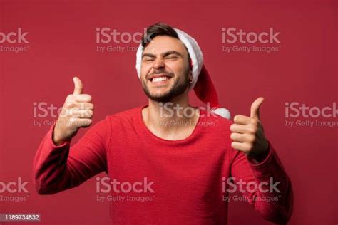 빨간 스웨터와 산타 모자를 입은 젊은 잘생긴 백인 남자가 스튜디오에서 빨간 배경에 서서 엄지 손가락을 보여줍니다 T 셔츠에 대한 스톡 사진 및 기타 이미지 Istock